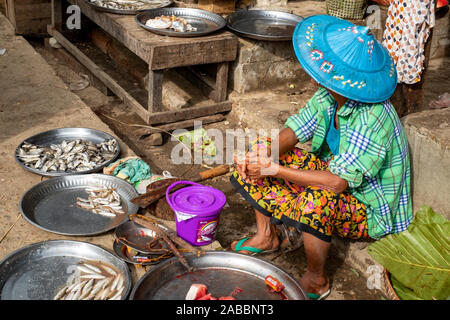 Female fishmonger in traditional conical Asian hat & sarong prepares ...