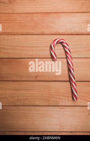 Beautiful striped hard candy cane staff on a wooden table and red wall ...