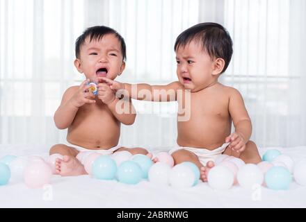 two twin babies crying on a bed Stock Photo - Alamy