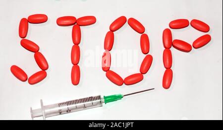 The word stop is laid out of tablets and a hand with a syringe which ...