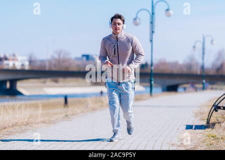 A panting athlete running fast on a track while wearing headphones and ...