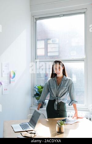 Woman standing behind desk in studio workspace, holding DSLR camera ...