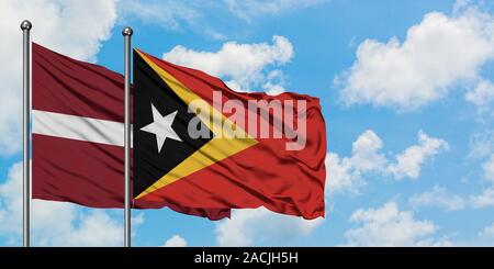 East Timor and Latvia flag waving in the wind against white cloudy blue ...