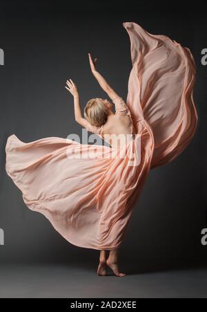 Woman in light chiffon dress dancing sensually on black plain ...
