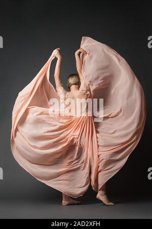 Woman in light chiffon dress dancing sensually on black plain ...
