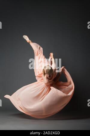 Woman in light chiffon dress dancing sensually on black plain ...