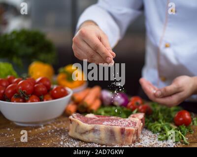 Master Chef hands putting salt on juicy slice of raw steak with ...