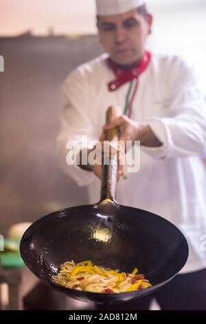 Young male chef flipping vegetables in wok at commercial kitchen Stock ...