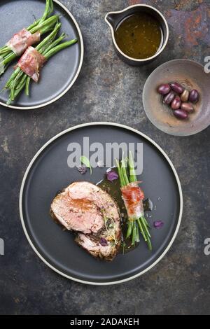 Kalamata black olives in a modern white plate with two olive leaves and ...