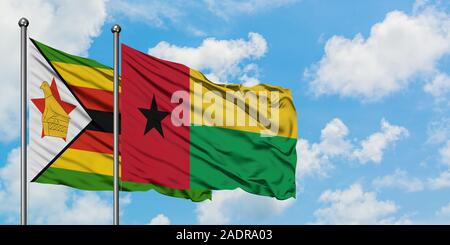 Zimbabwe and Guinea flag waving in the wind against white cloudy blue ...