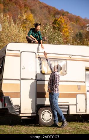 A woman sitting on the roof of a camper van in the forest against a ...