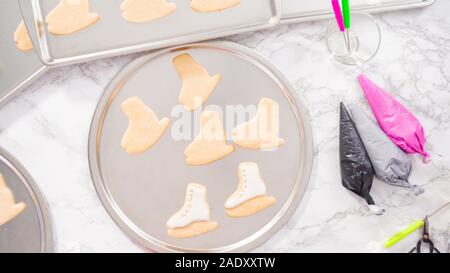 Flat lay. Decorating ice skate shaped sugar cookies with black color ...