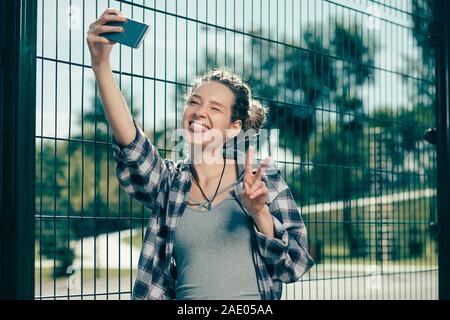 Pretty lady smiling while taking selfies near the chain link fence ...