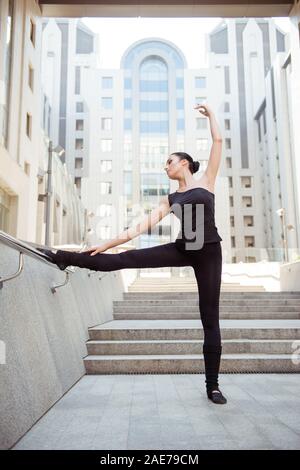 Girl standing at railing in ballet hall. Young ballerina stretching out ...