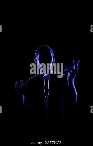 Silhouette of a man singing into a microphone. A spot of light, a ...