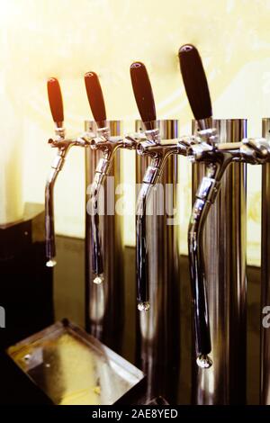 Row of shiny chrome beer taps with black handles, positioned above ...