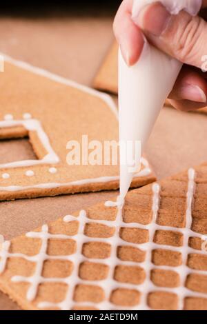 Woman is decorating gingerbread cookies house with white frosting icing ...