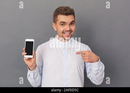 Young handsome man showing smartphone screen pointing and showing with ...