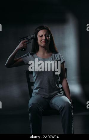 crying, despaired woman holding gun near chin on dark background Stock ...