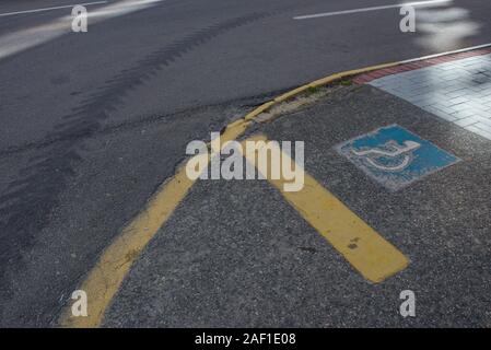 Wheelchair users symbol in a sidewalk, and tire marks on street corner ...