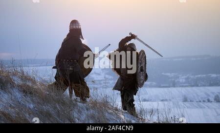 Two viking are fighting with axes and shields on the winter meadow ...
