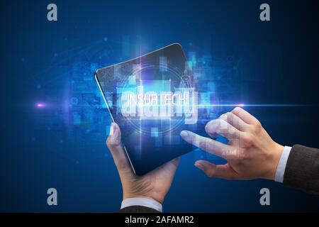 Businessman holding a foldable smartphone with INSURTECH inscription ...
