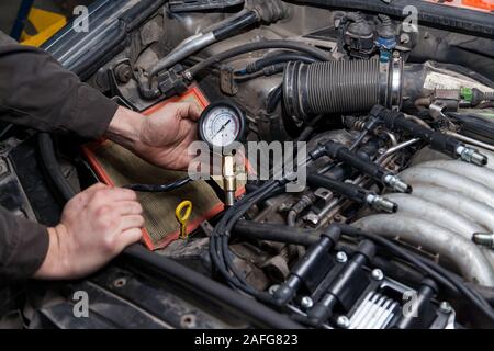 A male mechanic measures the compression in the cylinder of a car ...