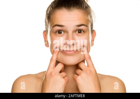 Young woman forcing her smile with her fingers on white background ...
