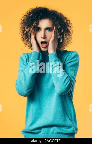 scared curly teenager with open mouth looking away isolated on yellow ...