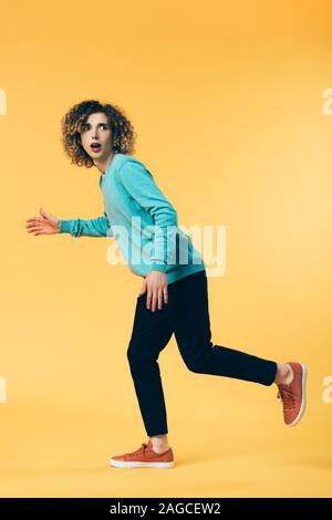 scared curly teenager with open mouth looking away isolated on yellow ...