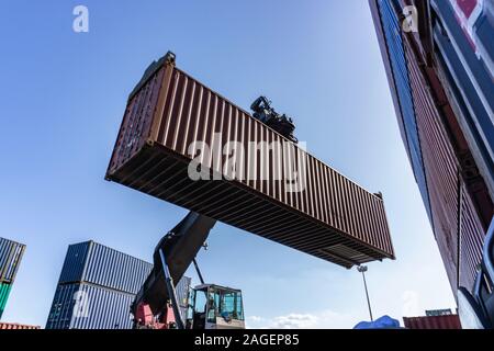 Reach stacker lifting a shipping container behind a wire mesh fence in ...