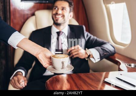 cropped view of flight attendant giving cup of coffee to handsome ...
