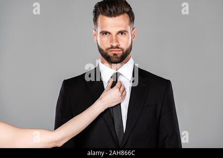 woman tying tie on handsome businessman in black suit isolated on grey ...