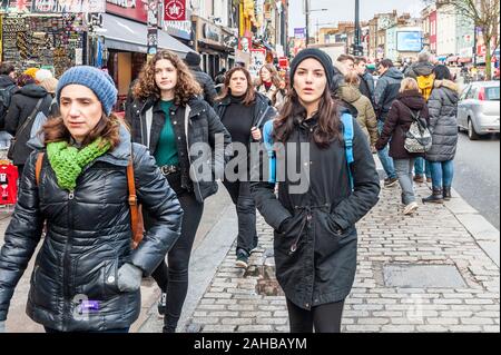 People walk along a street with high old stone walls with doorways as ...