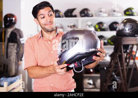 Smiling man is choosing moto helmet for head protection in sport shop ...