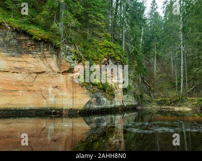 a landscape with a steep river and caves on a sandstone cliff, a cloudy ...
