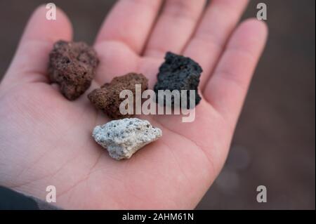 Hand holding different coloured lava rocks - white, brown and black ...