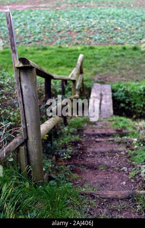 A small wooden footbridge over a ditch leads to a wooden gate in the ...