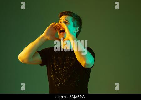 Calling somebody, screaming. Caucasian man's portrait isolated on green ...