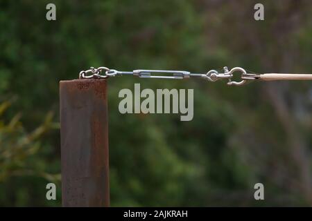 A stainless steel turnbuckle shackle connected to a black metal pole ...