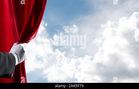 Cloudy landscape behind red curtain and hand holding it Stock Photo - Alamy