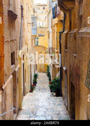 A narrow street in Valletta, Malta, in shadow, with a church dome in ...