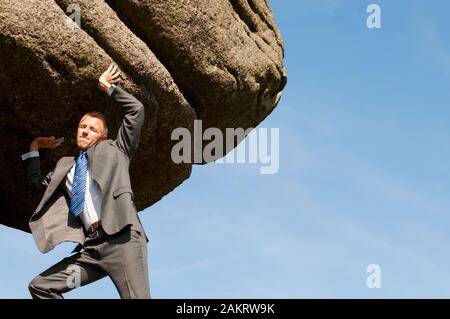 Strong businessman struggling to lift massive boulder into blue sky ...