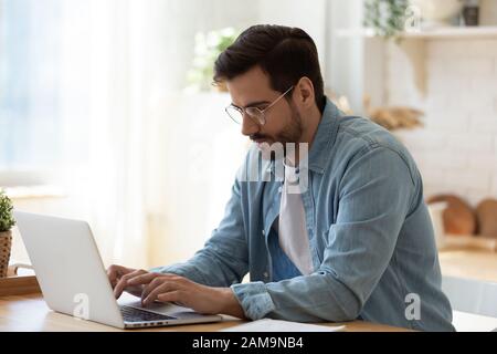 handsome young programmer in eyeglasses and headphones working with laptop and desktop computer ...