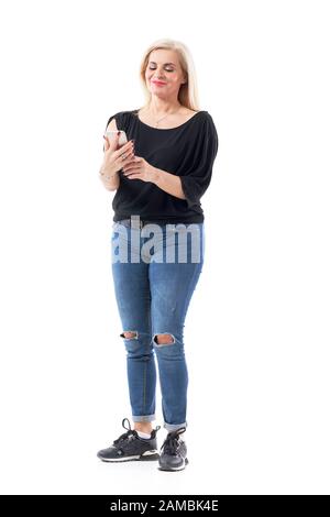 Senior blond woman surfing the net through mobile phone while standing ...