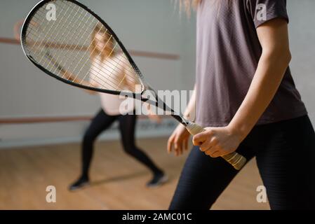 Two female players with squash rackets sits back to back on court floor ...