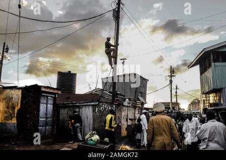 A local electrician climbs over an electric pole in Kibera Slums.Lack ...