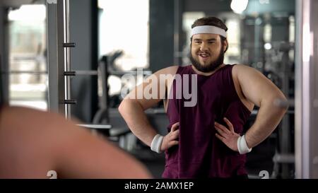 Funny fat man looking at mirror reflection gym and posing, pretending ...
