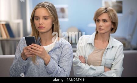Daughter with smartphone in hands ignoring her mom, indifference ...