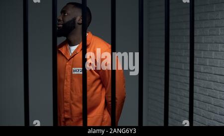 Black male prisoner waiting for sentence in prison cell, looking sadly ...